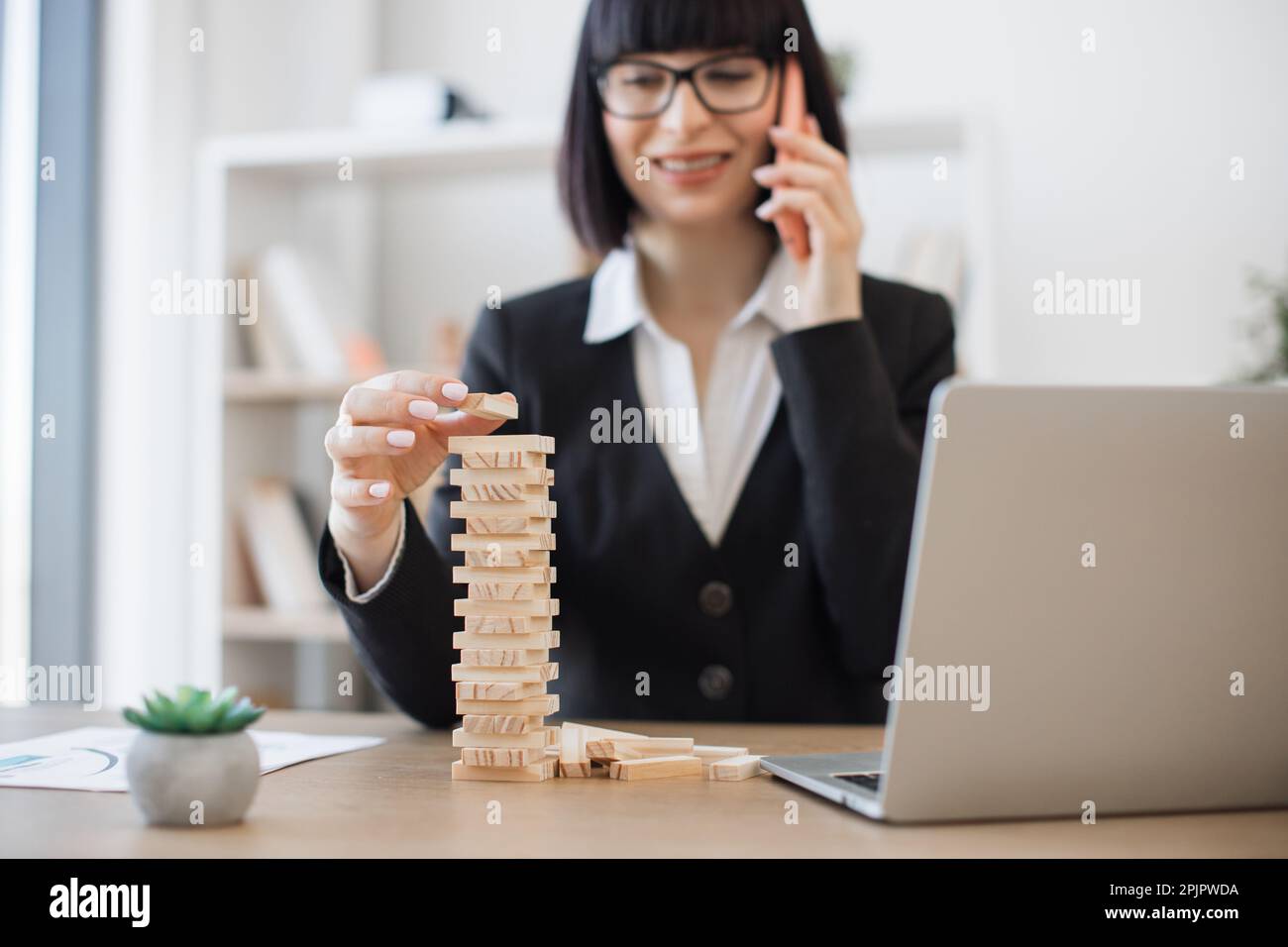 Young caucasian businesswoman in glasses holding wooden block of jenga ...