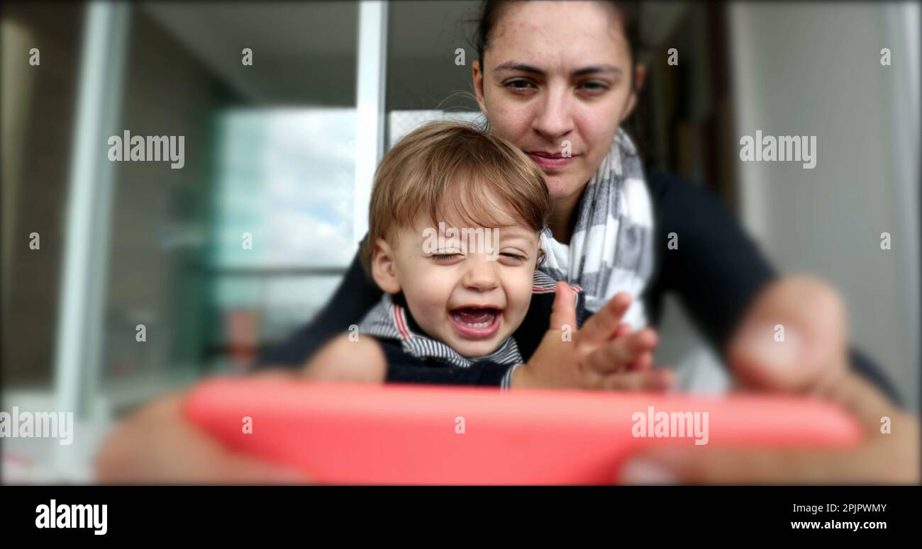 Toddler boy clapping hands while on mom lap watching smartphone screen ...