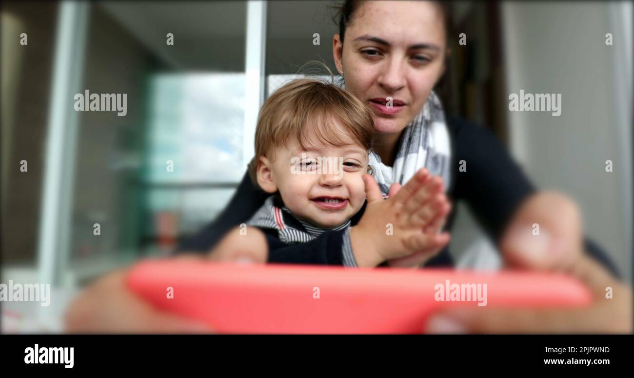 Toddler boy clapping hands while on mom lap watching smartphone screen ...