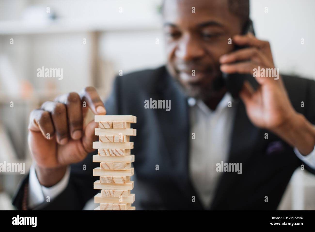 Happy multicultural man in business suit playing jenga while talking on ...