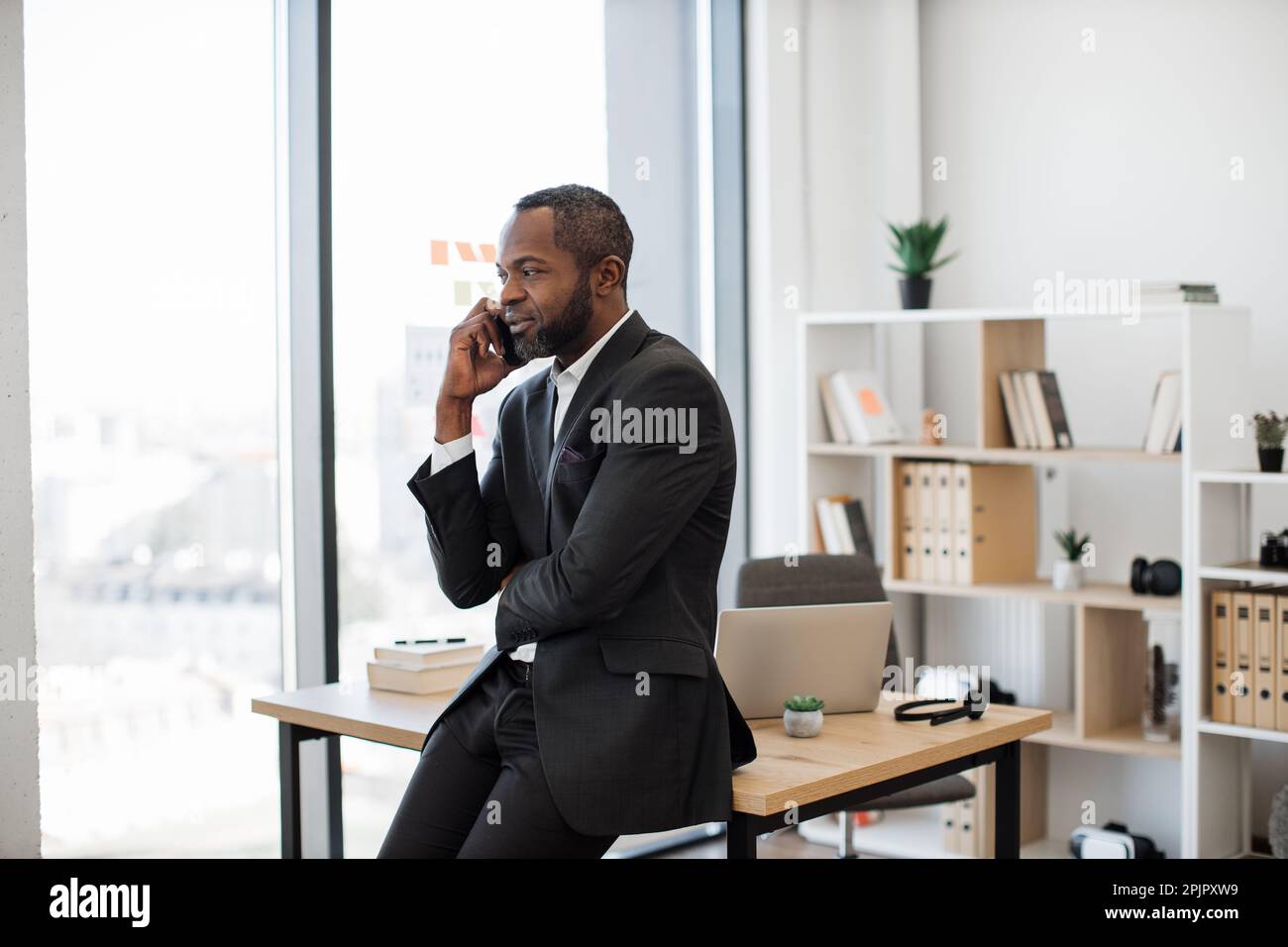 Confident african american businessman in formal attire speaking on cell phone while leaning ...