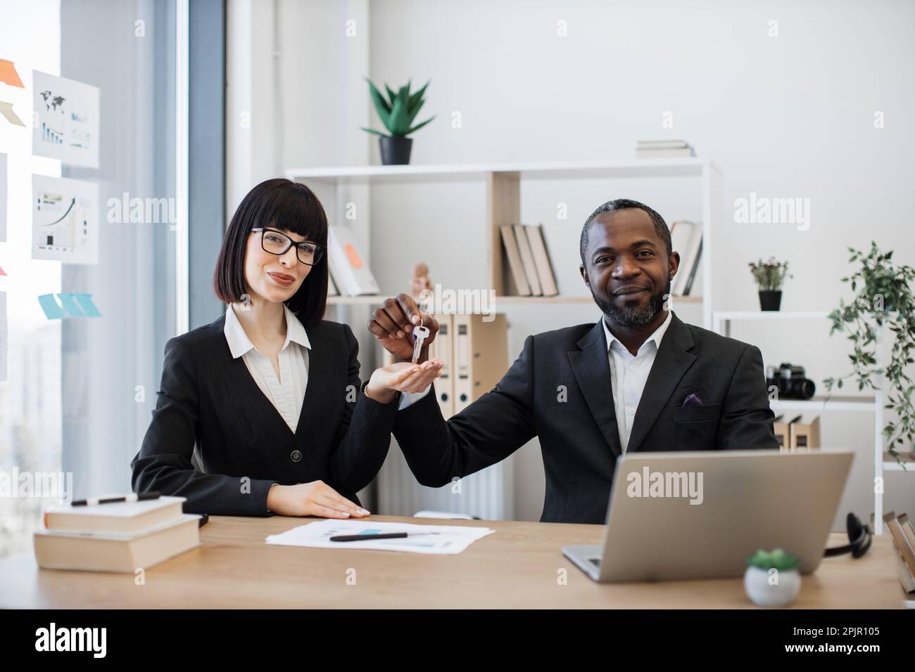 Professional managing brokers in formal clothes sitting in real estate agency with keys in hands ...