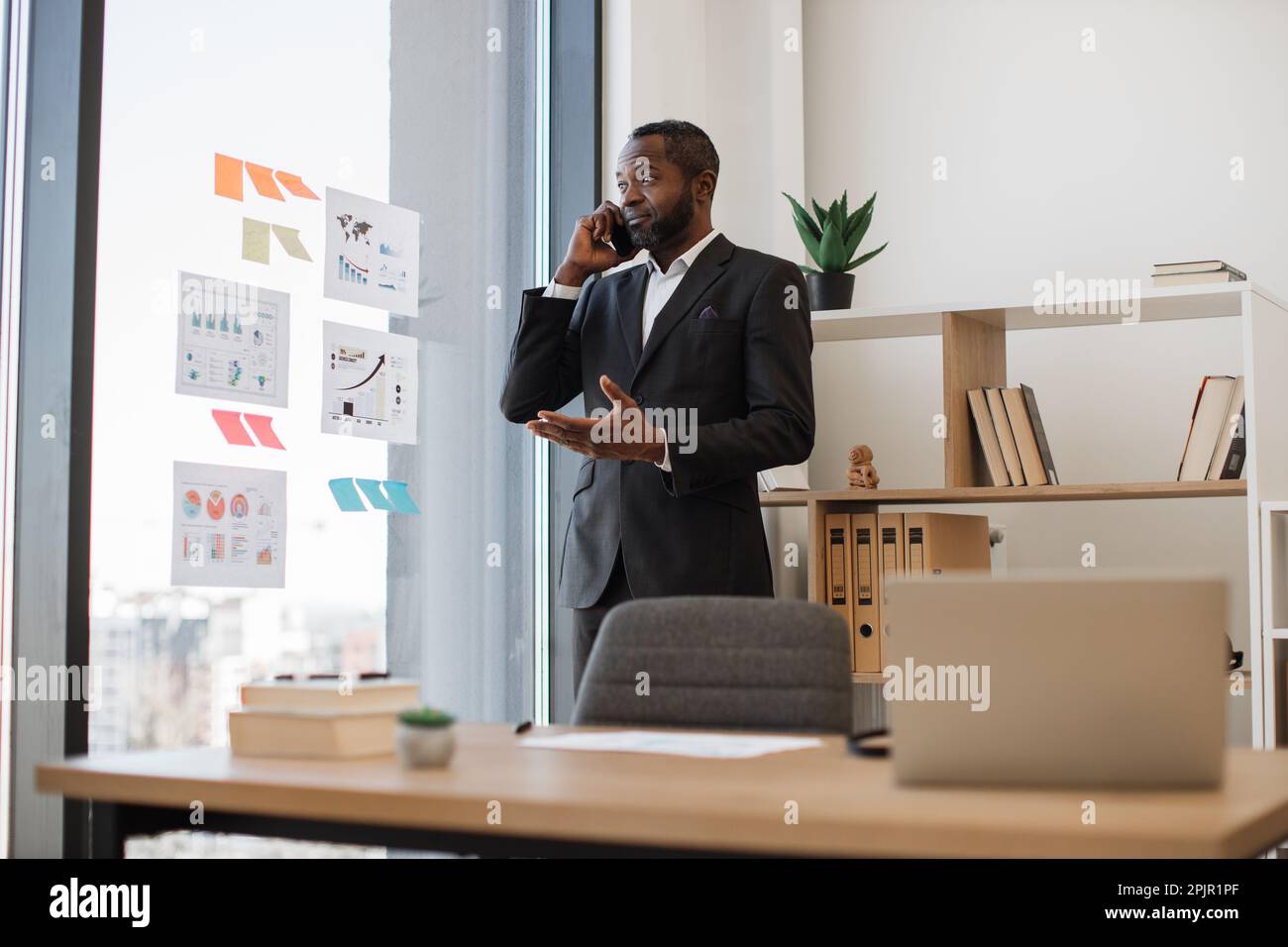 Multiethnic businessperson in formal outfit having conversation on cell phone while standing out ...