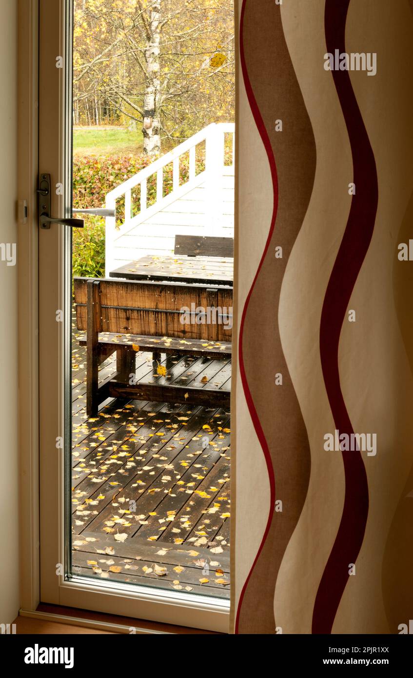 View through a patio door into an autumn-wet balcony. Leaves, furniture ...