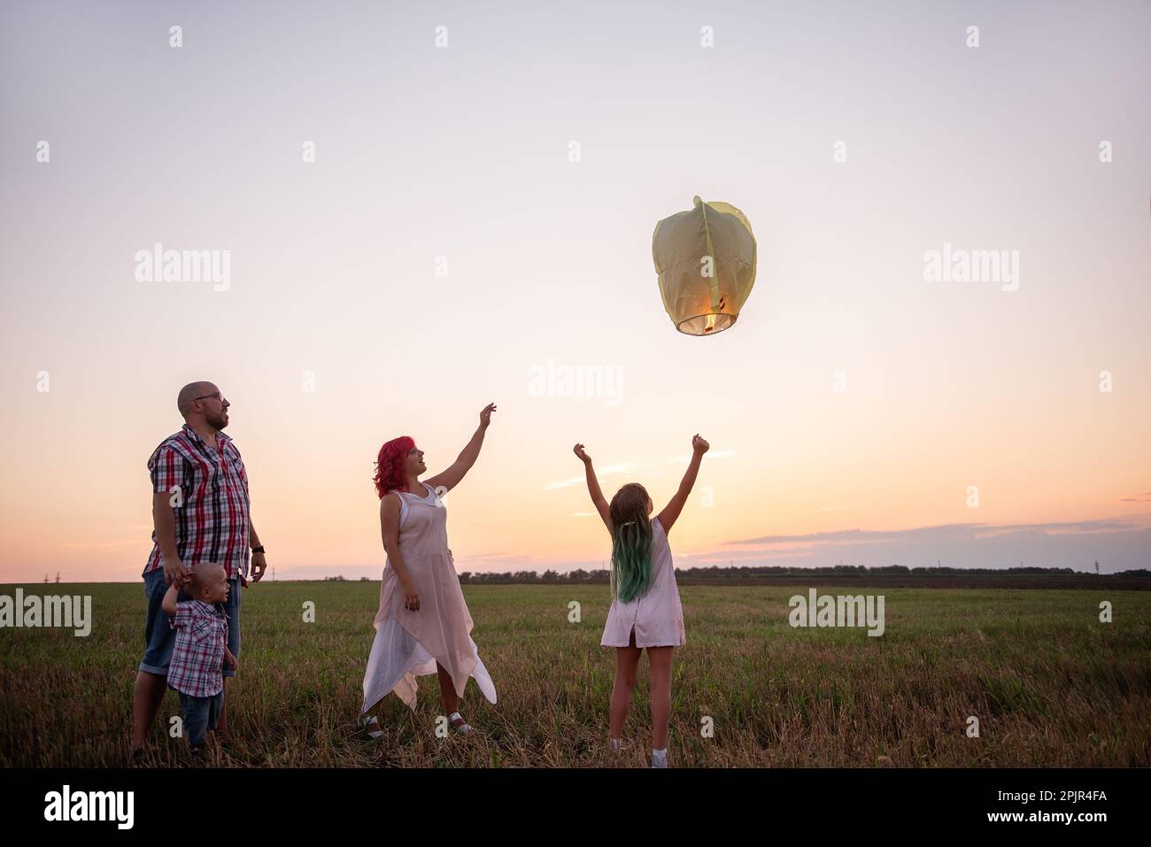Diversity family launch yellow sky lantern in field at sunset. Mother ...