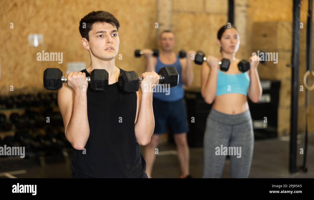Young dedicated active strong fit man doing exercises for shoulders ...