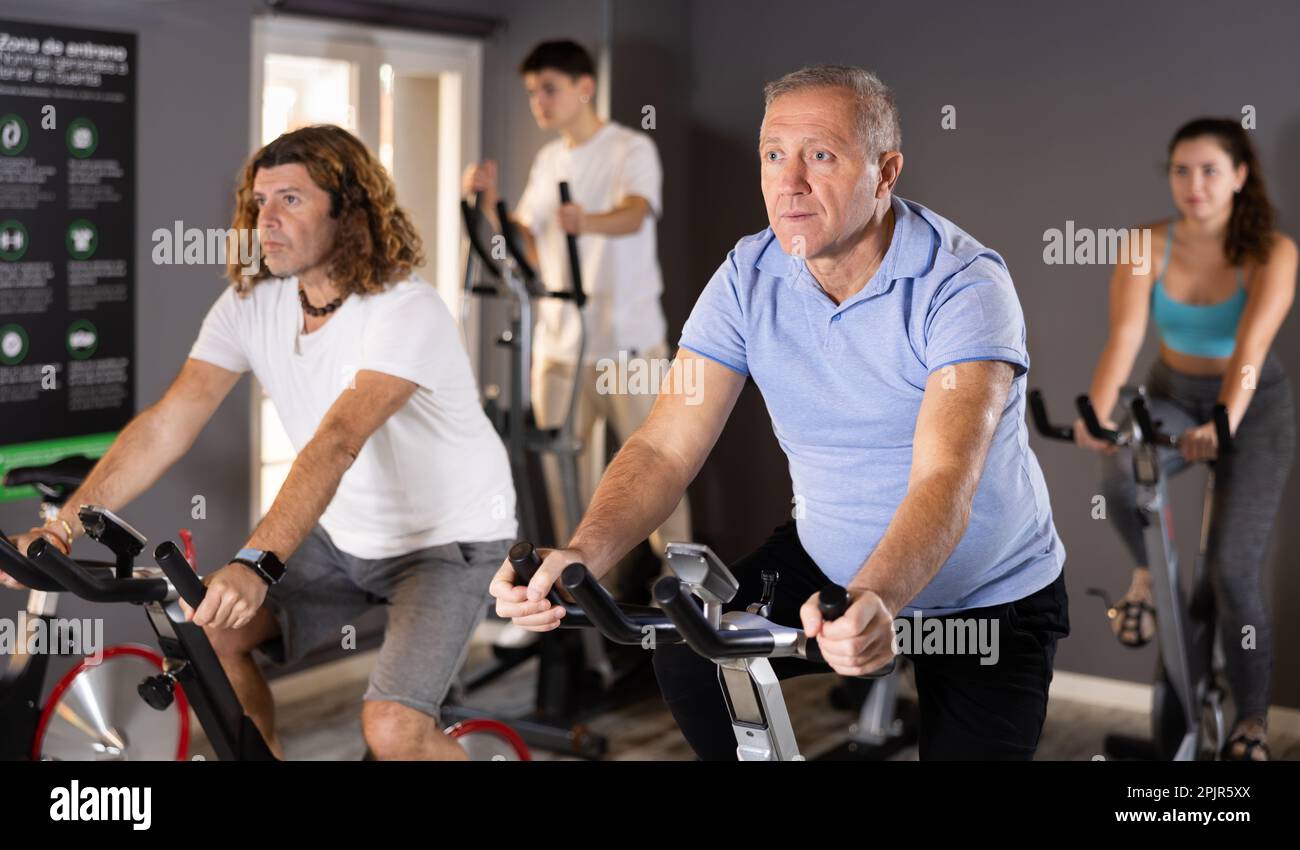 Positive mature male riding exercise bike during cycling class in gym ...