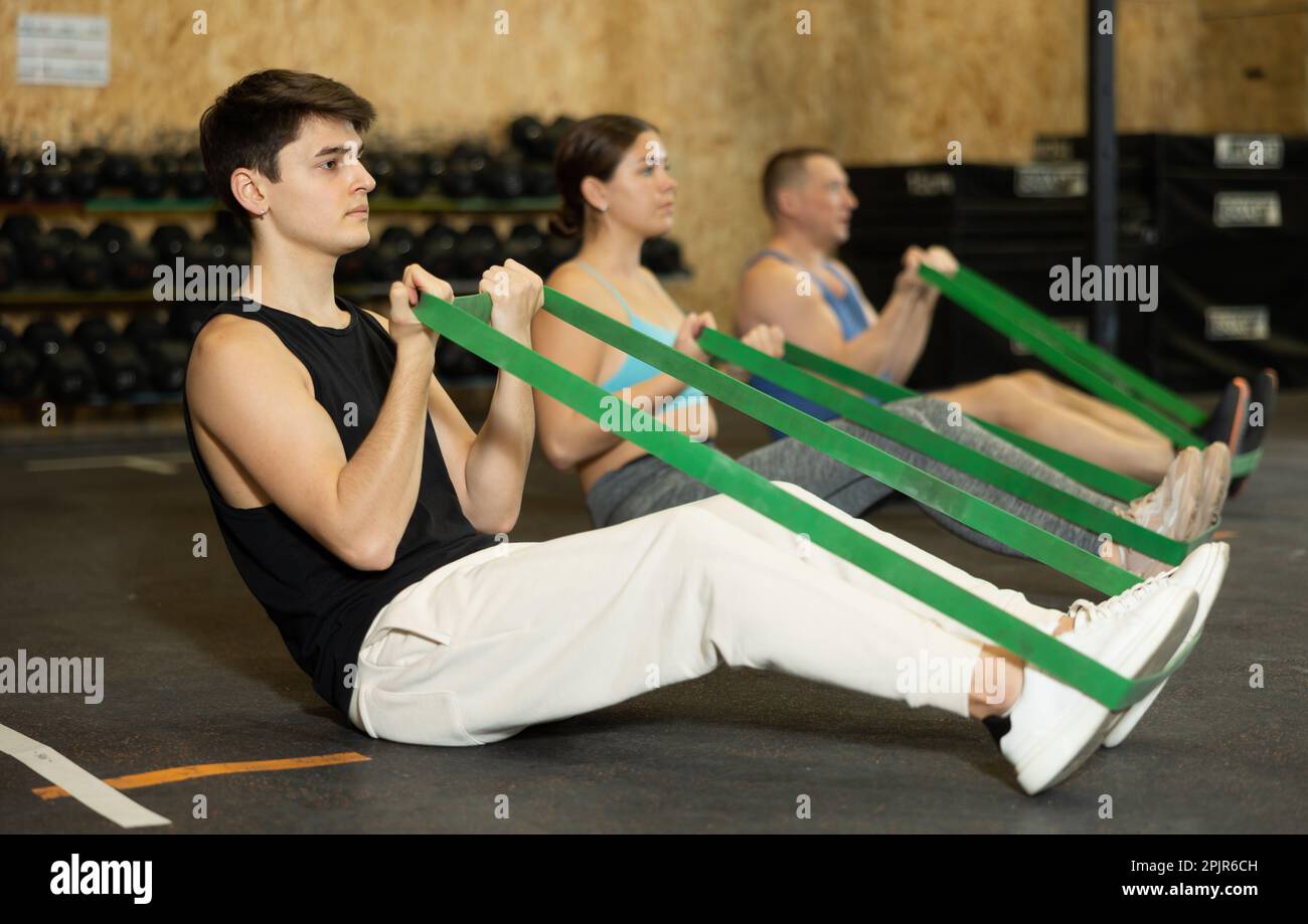 Motivated young man practicing exercises with stretch rope sitting near ...