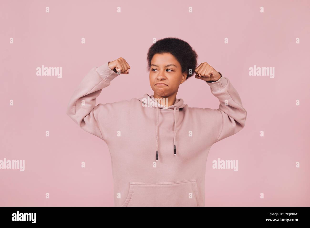 Brave student girl in hoodie posing on pink backdrop. Strong black ...