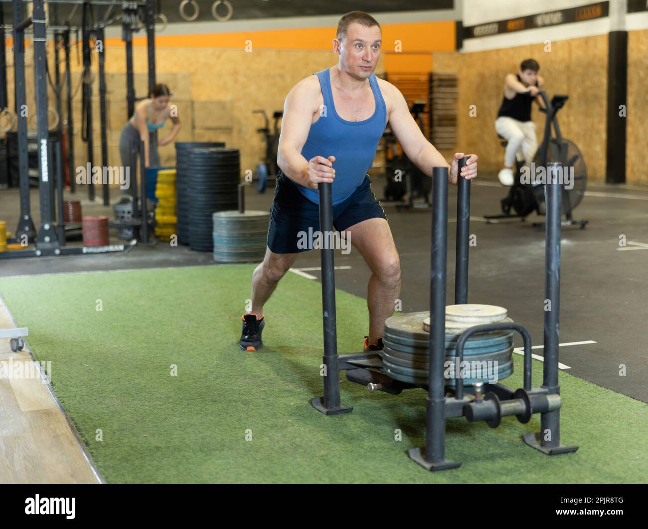 Concentrated man pushing heavy sled during intense training in gym ...