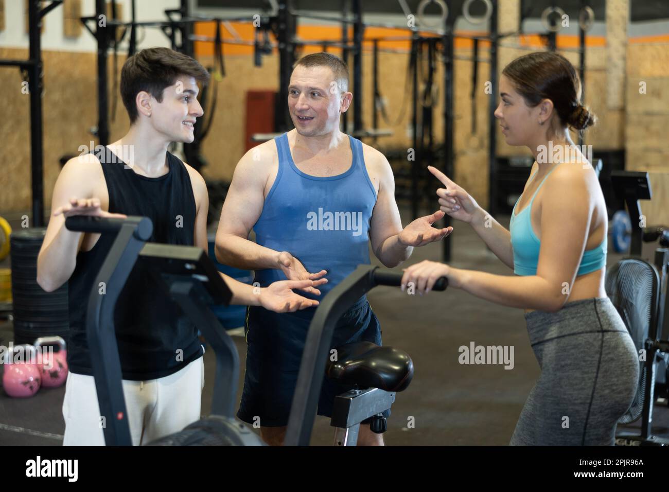 Positive sporty man talking friendly to girl and guy in gym Stock Photo ...