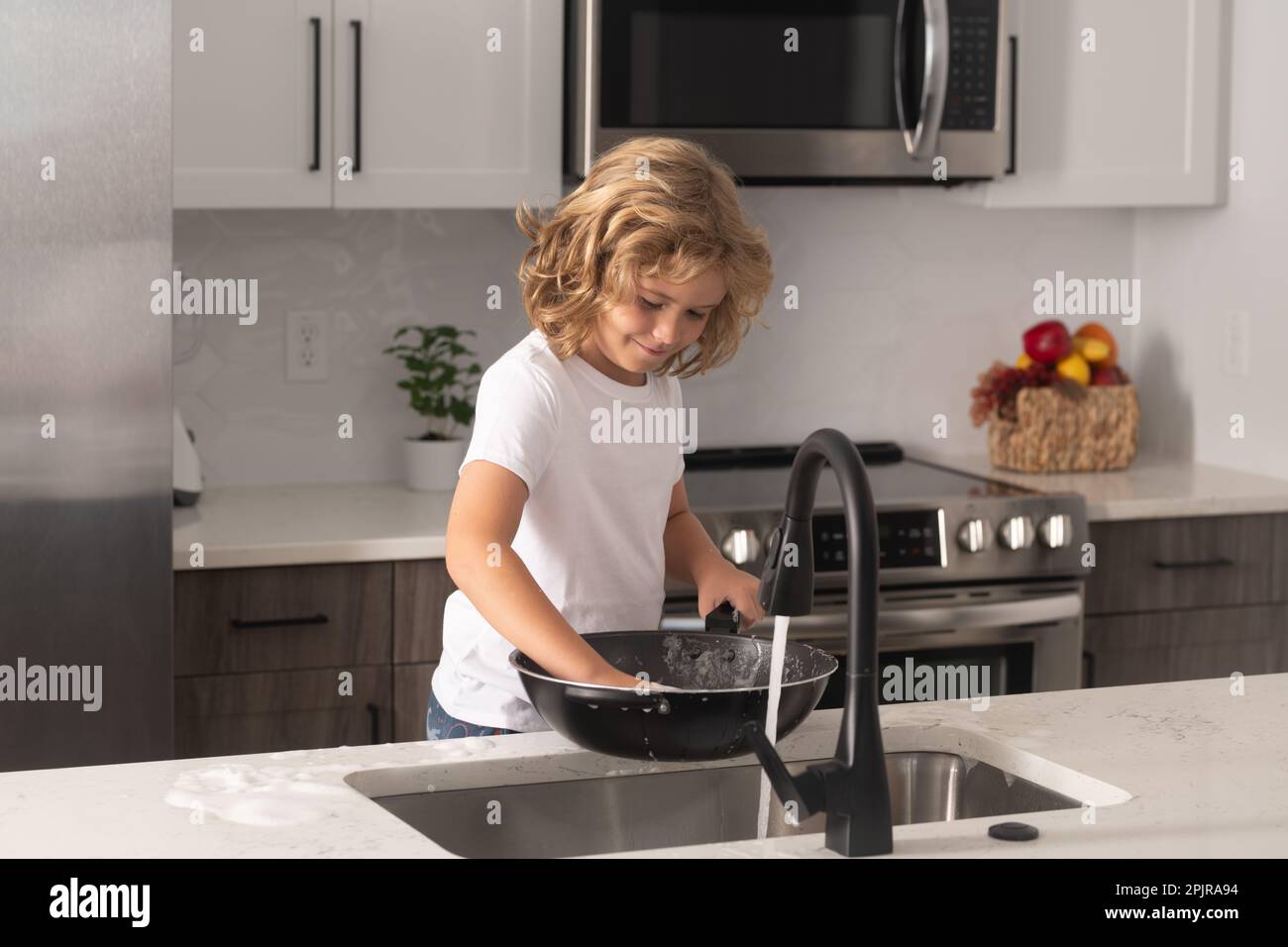 Home chores. Kid in kitchen cleaning plates. Cute boy washing dishes in ...