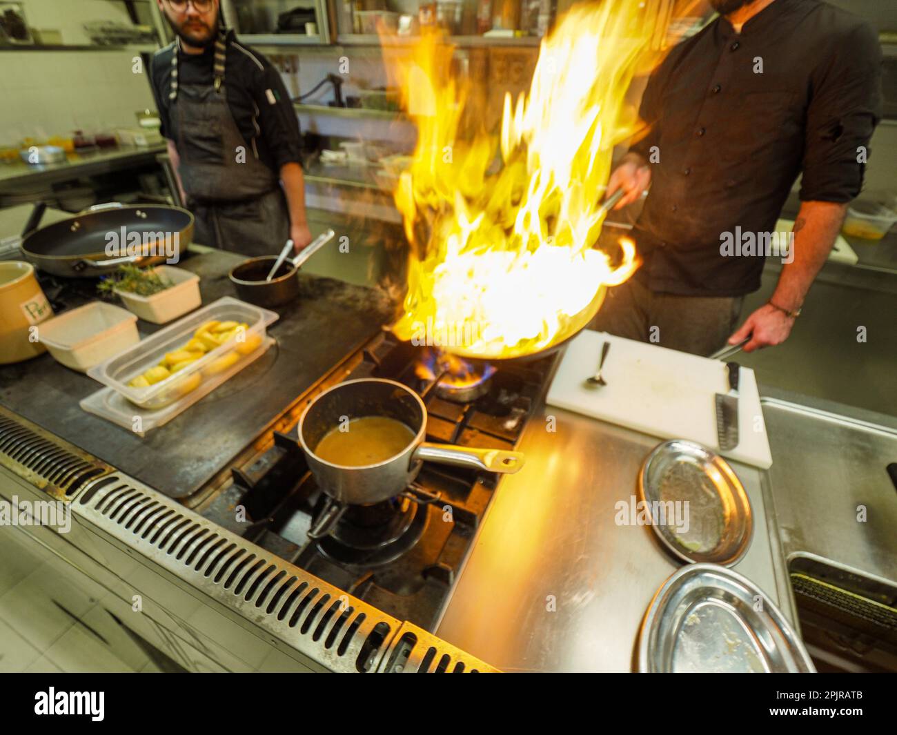 Chef cooking flambleing atlantic squid with olive oil in a big pan in a ...