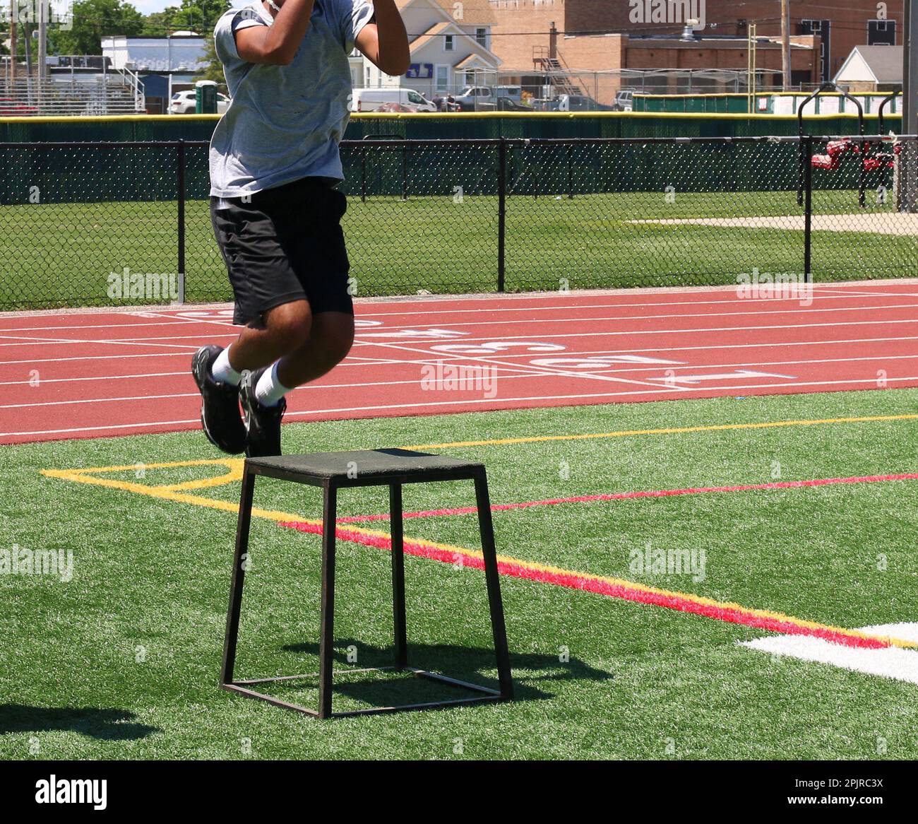 A high school boy is in the air jumping on to a plyos box on a green ...