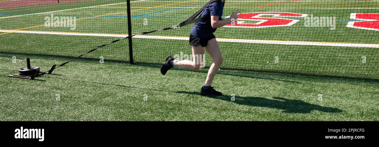 Side view of a high school runner is pulling a sled that has weights on ...