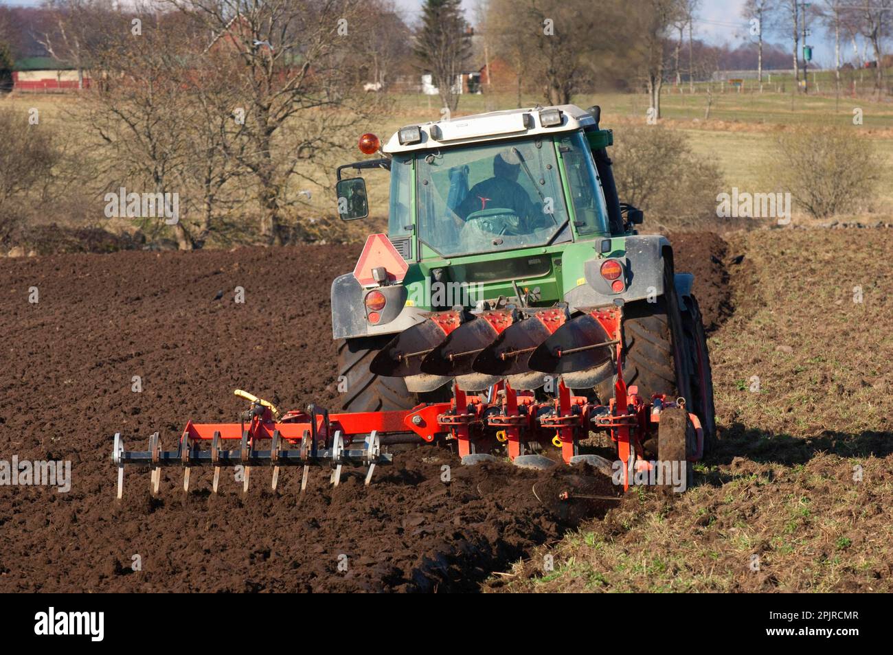 Tractor pulling a four-furrow reversible plough and a small harrow ...