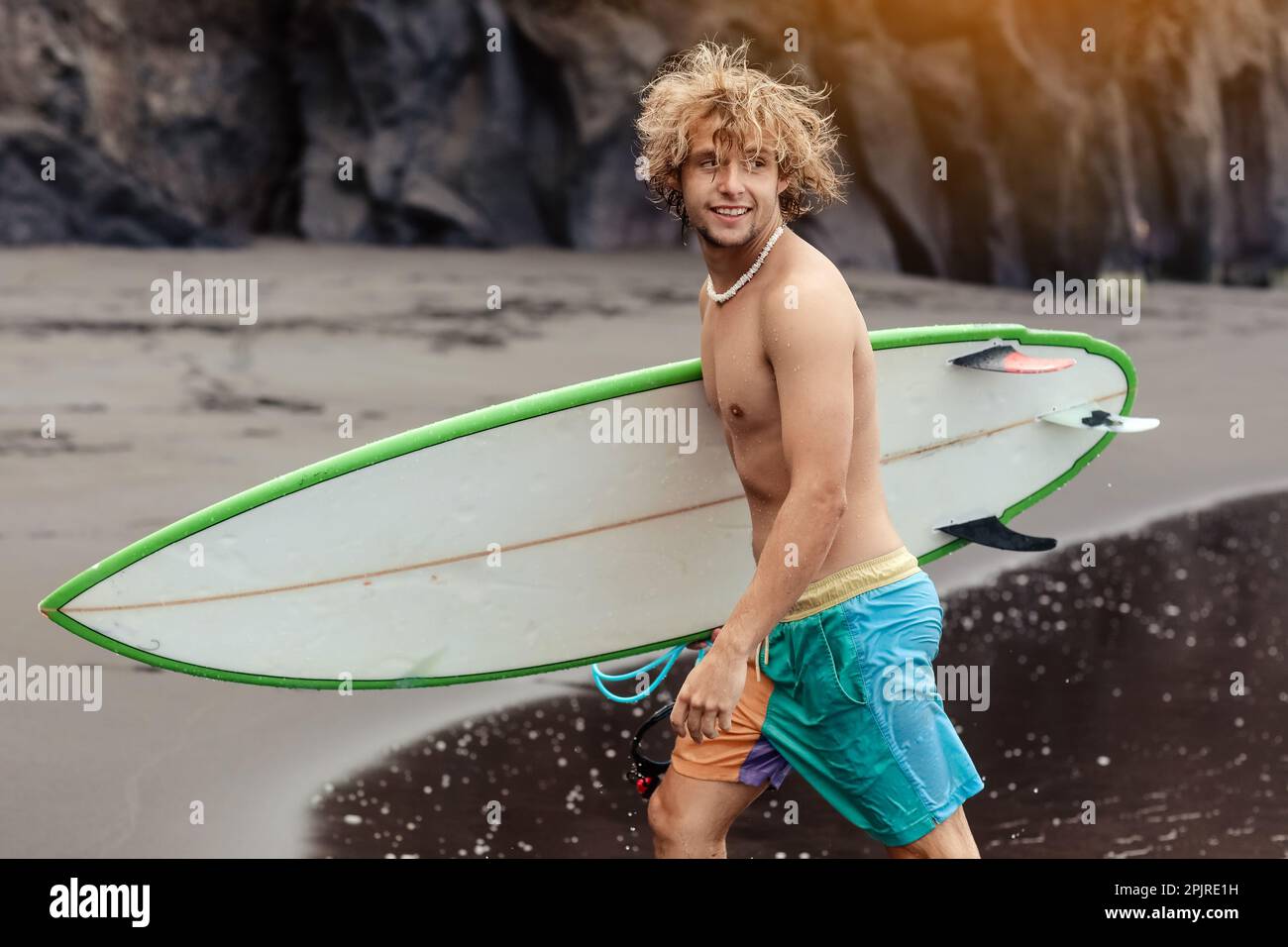 Fit young surfer man with curly blond hair with surfboard goes by the ...