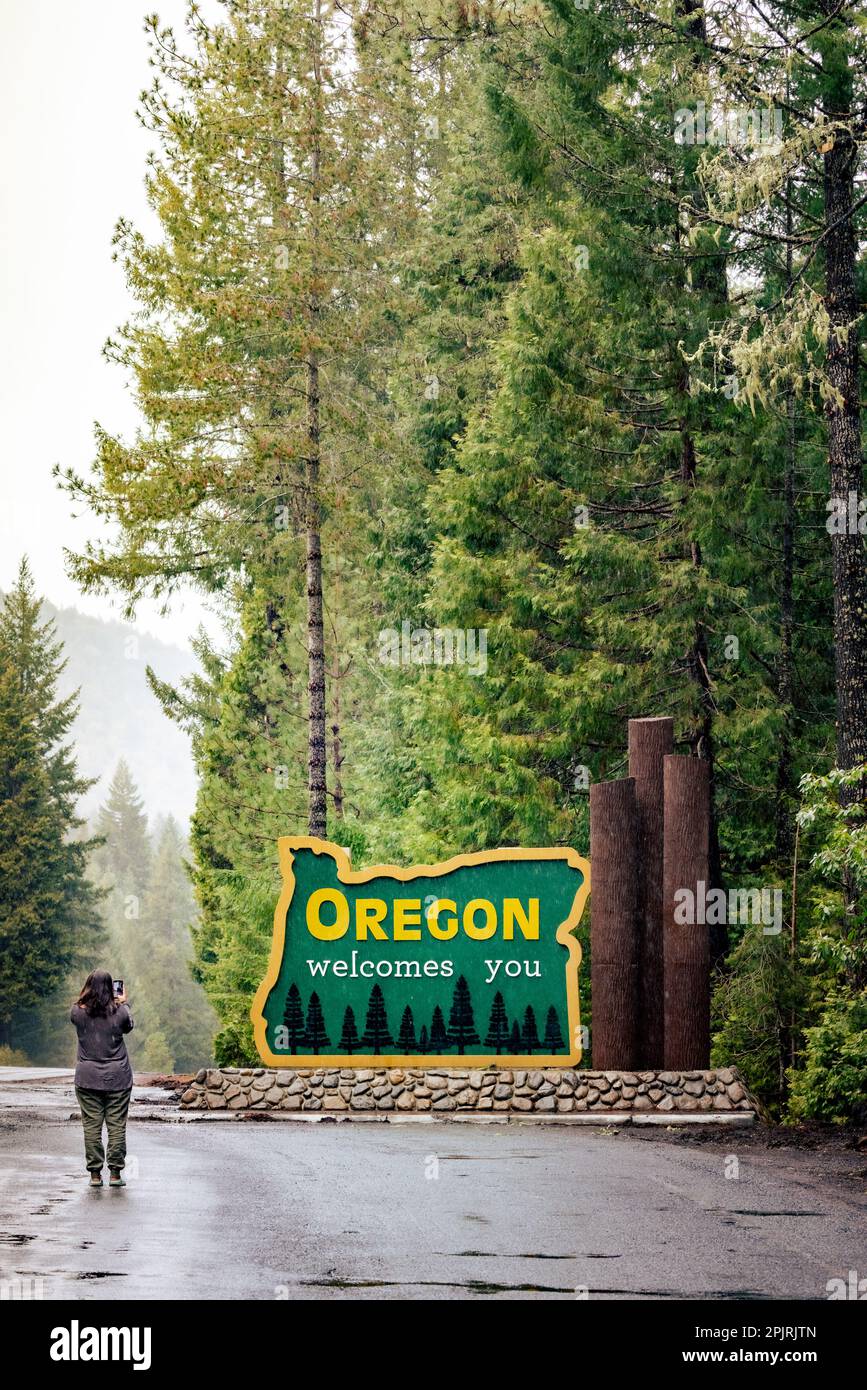 Vertical photo of woman taking photo of Oregon welcomes you sign on HWY ...