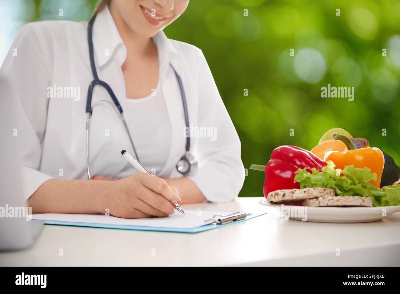 Nutritionist working at table on blurred green background, closeup ...