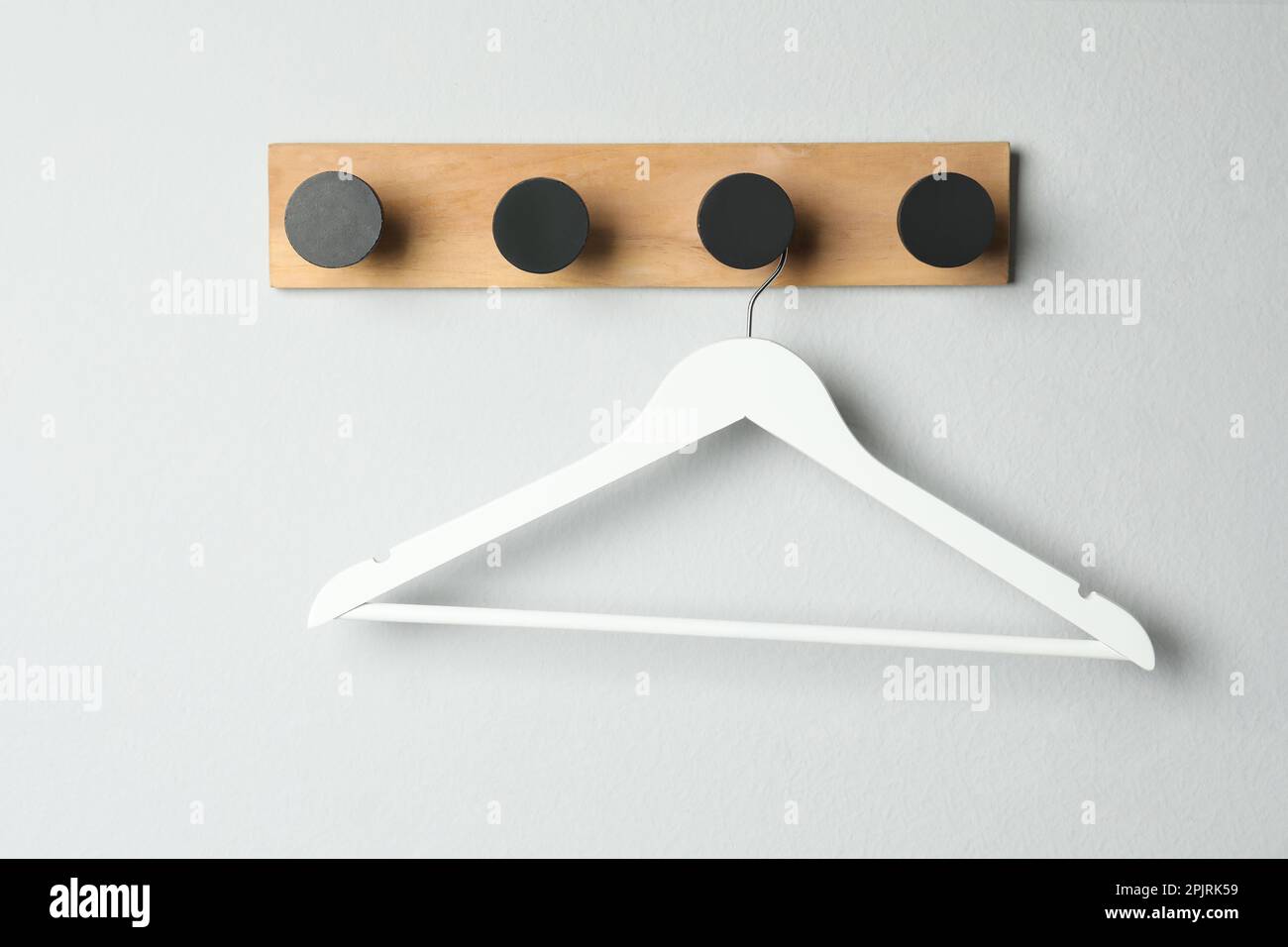 Rack with empty clothes hanger on white wall Stock Photo - Alamy
