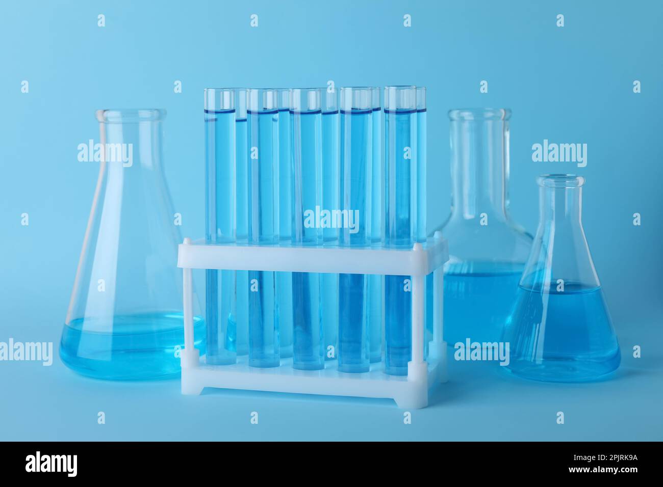 Laboratory glassware with light blue liquid on turquoise background ...
