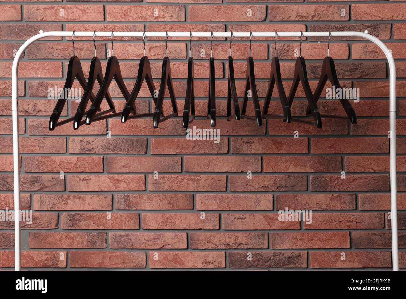Black clothes hangers on rack near red brick wall. Space for text Stock ...
