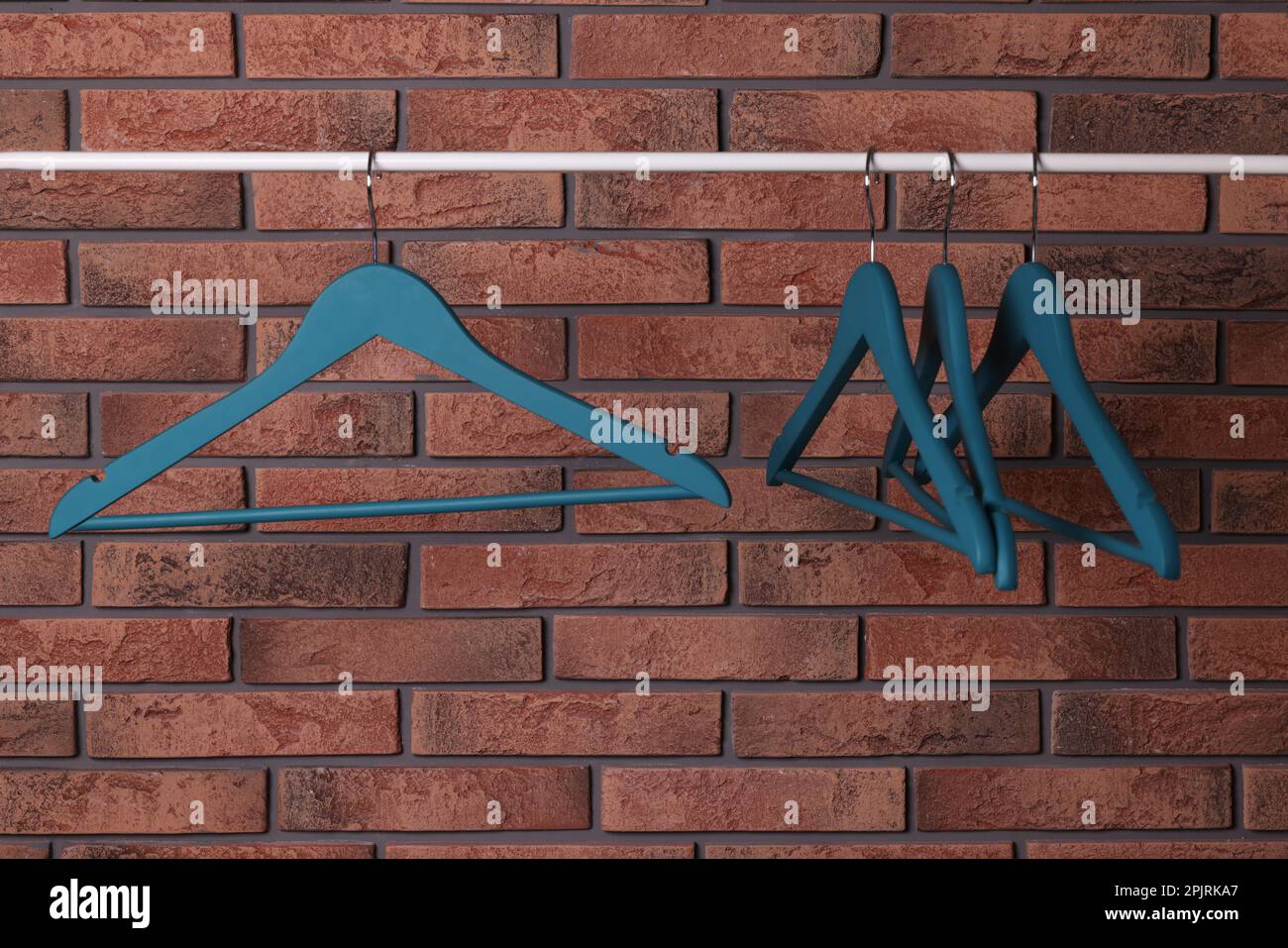 Blue clothes hangers on rail near red brick wall Stock Photo - Alamy