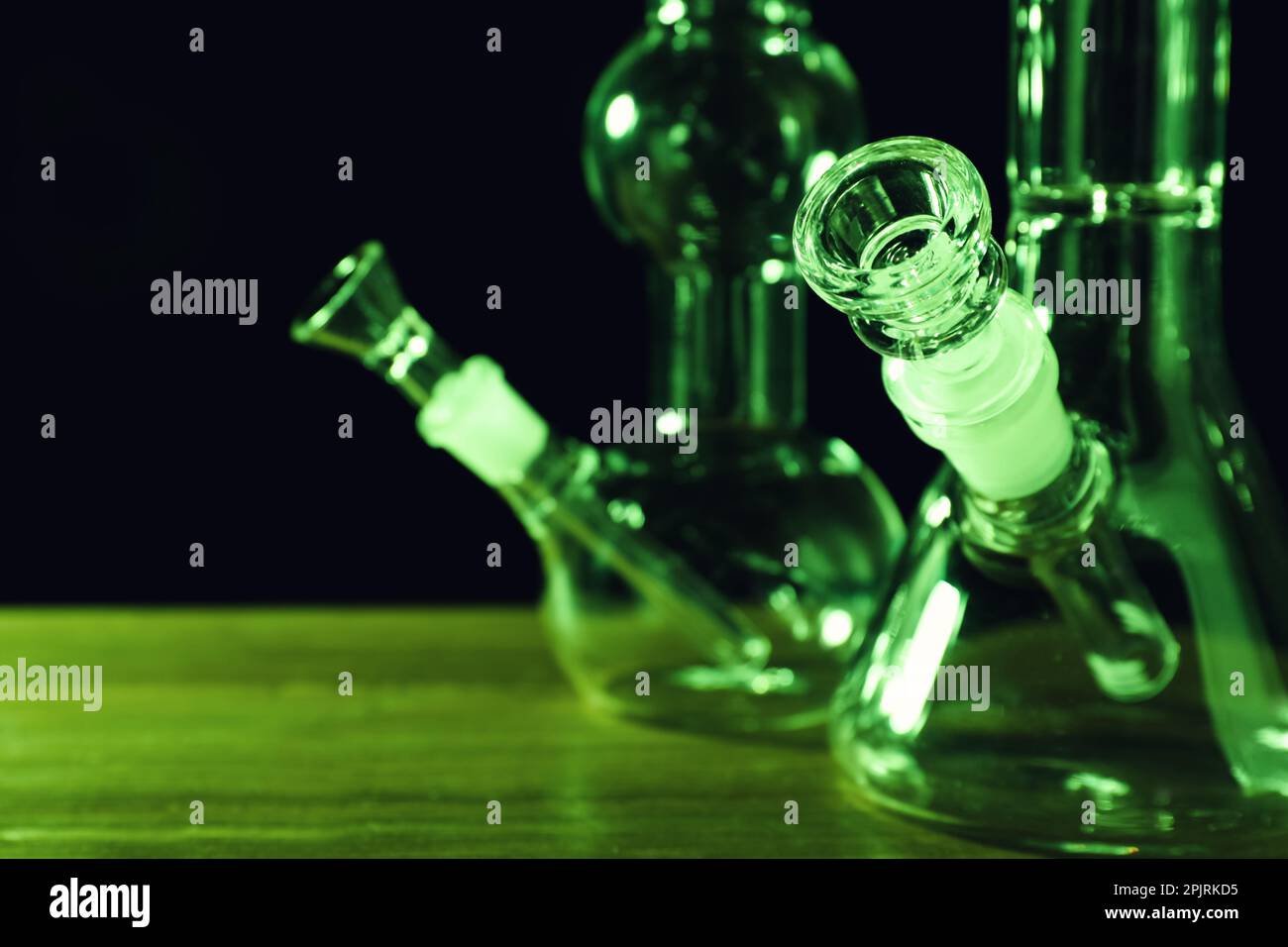 Glass bongs on wooden table against black background, toned in green ...