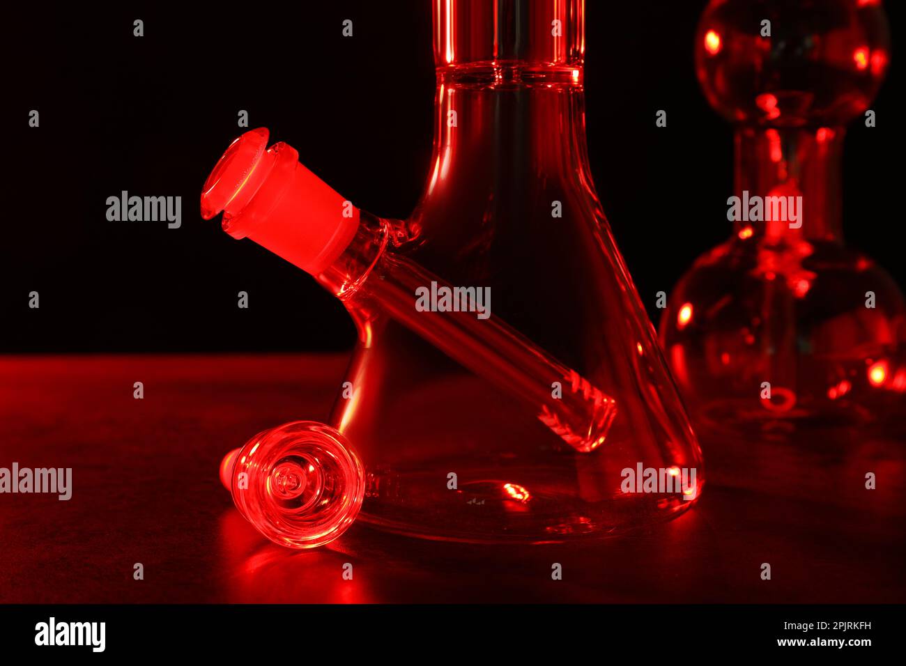 Glass bongs on table against black background, toned in red. Smoking ...