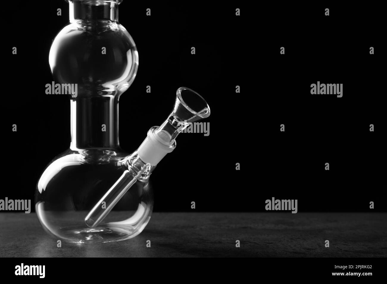 Glass bong on grey table against black background, space for text ...