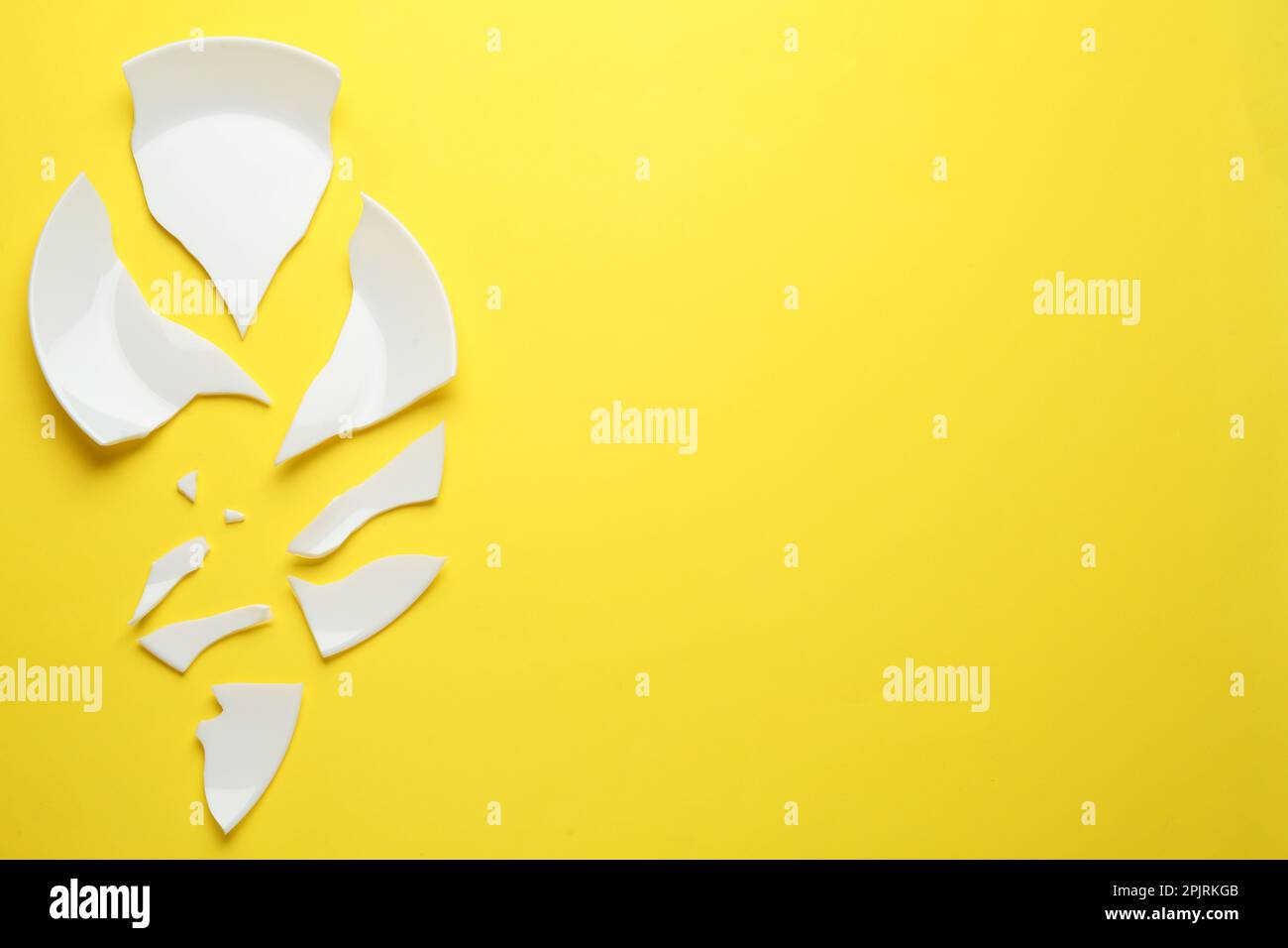 Pieces of broken ceramic plate on yellow background, flat lay. Space ...