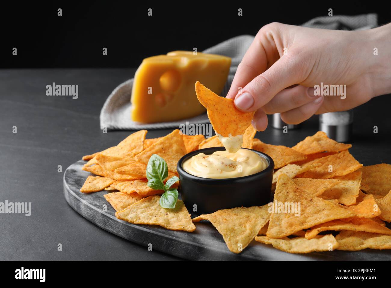 Woman dipping crispy nacho into delicious cheese sauce at black table ...