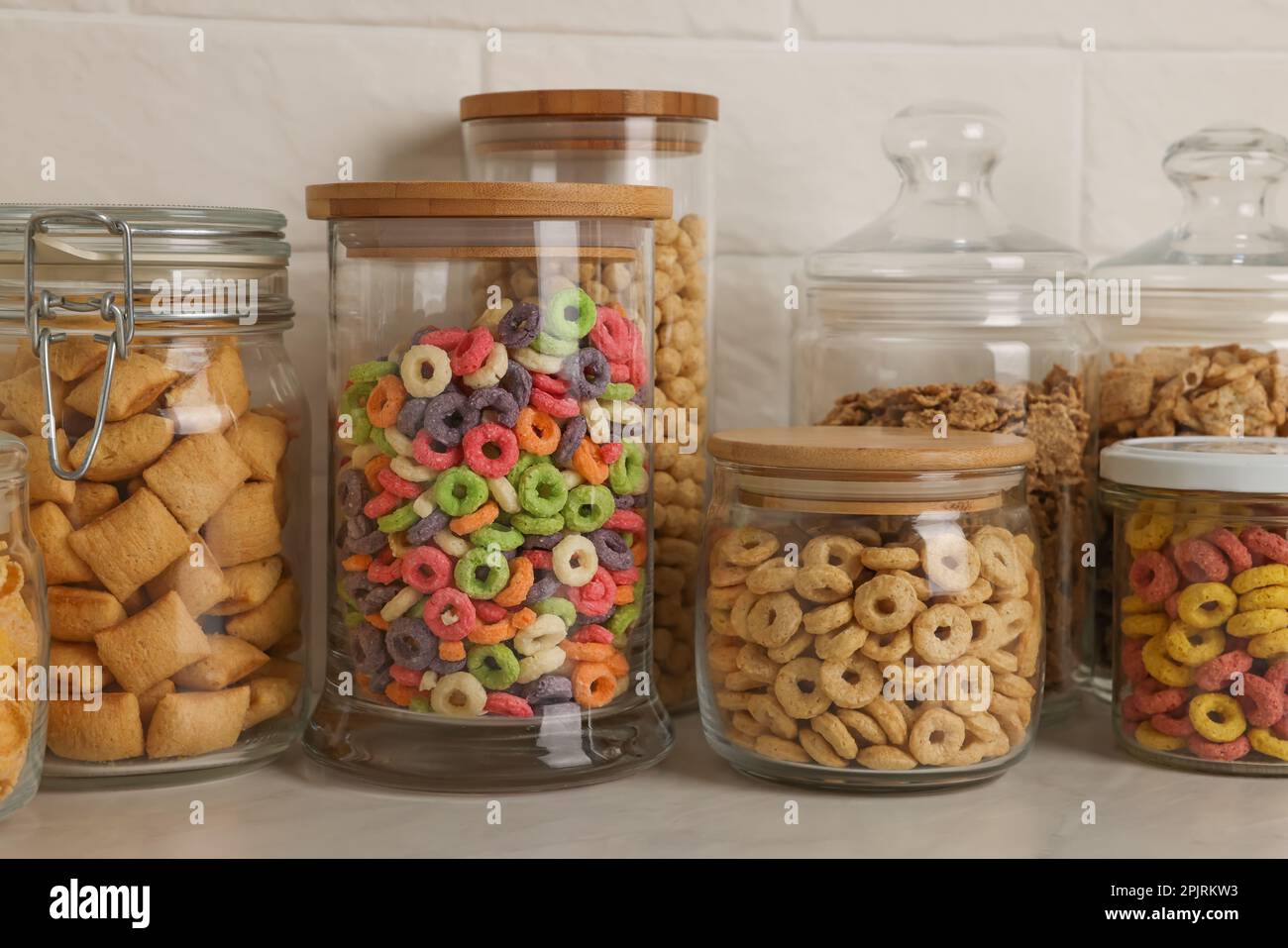 Glass containers with different breakfast cereals on white countertop ...