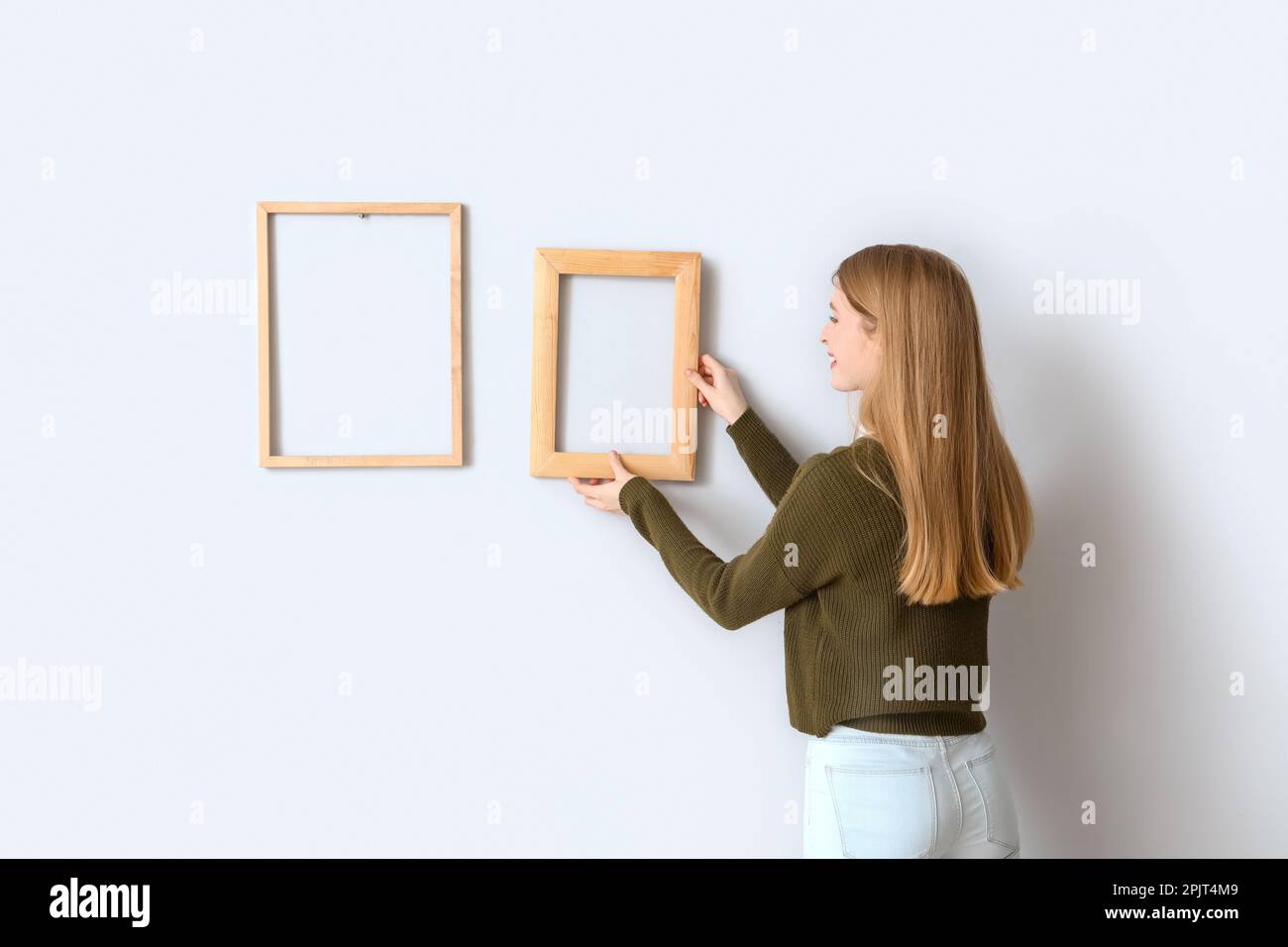 Young woman hanging frame on light wall Stock Photo - Alamy