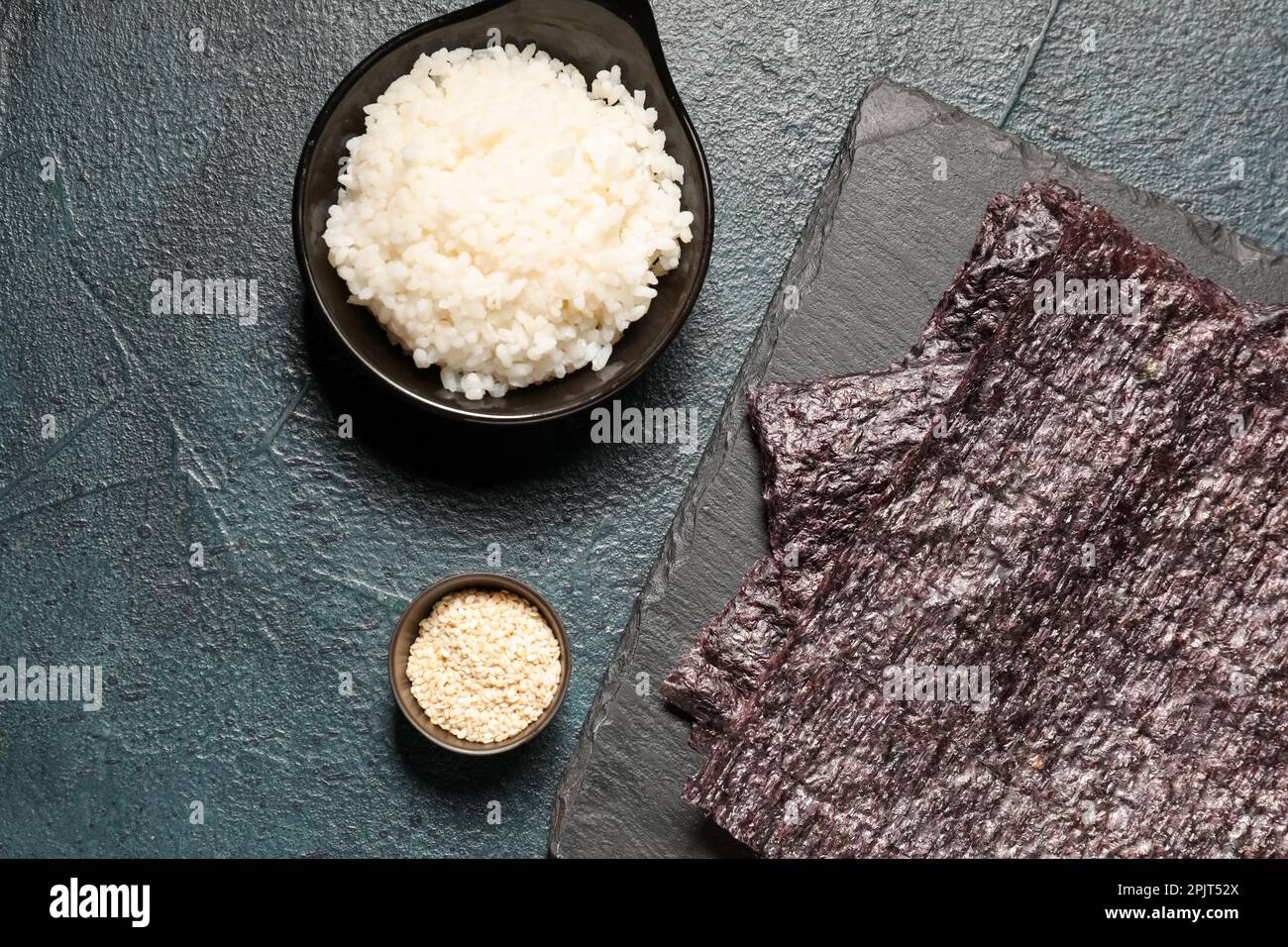 Slate board with nori sheets, rice and sesame seeds on dark color ...