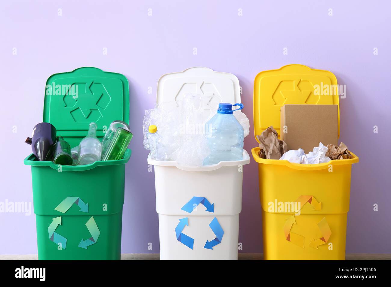 Containers with different types of garbage on lilac background ...
