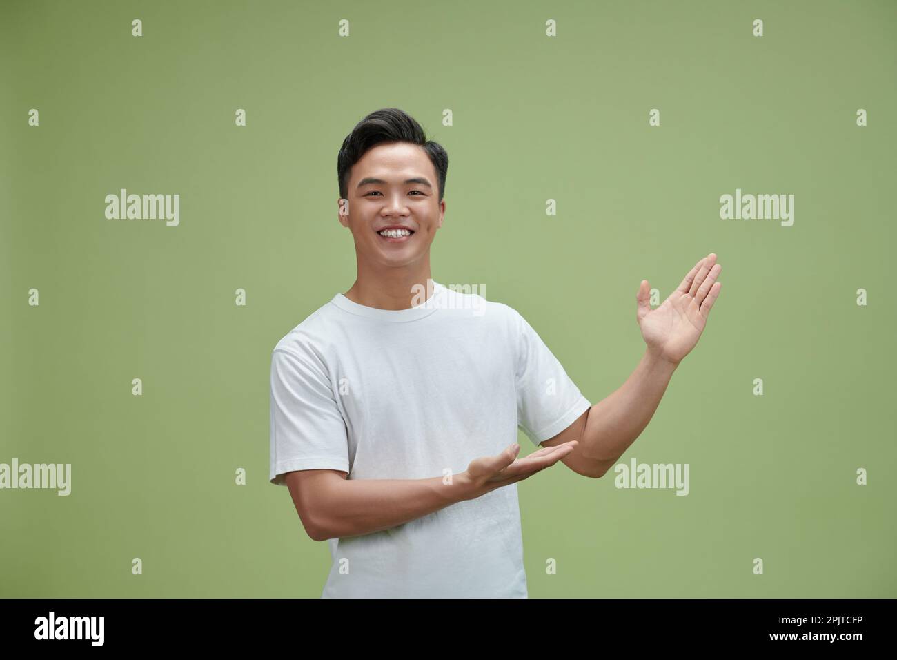 happy young asian man showing something imaginary over green background ...