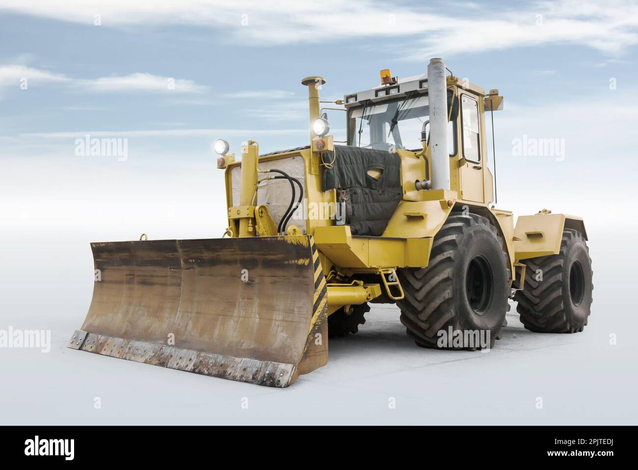 Yellow heavy wheeled tractor isolated on bright background with sky ...