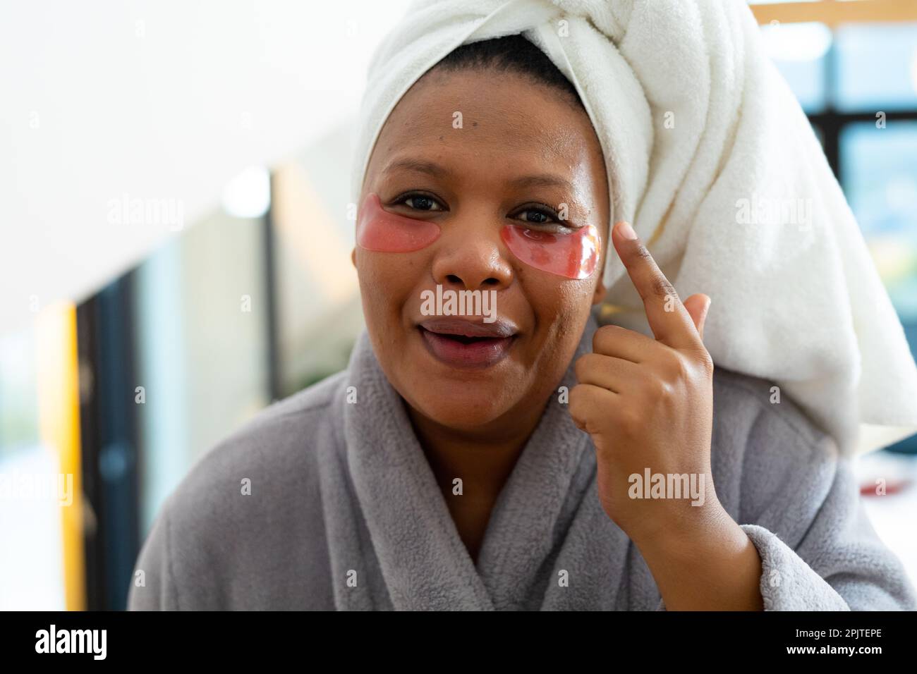 Happy plus size african american woman wearing robe, applying eye masks ...