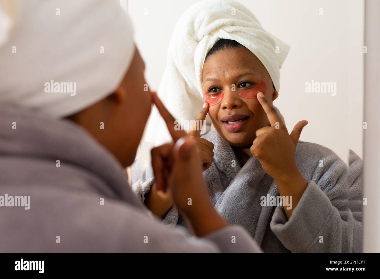 Happy plus size african american woman wearing robe, applying eye masks ...