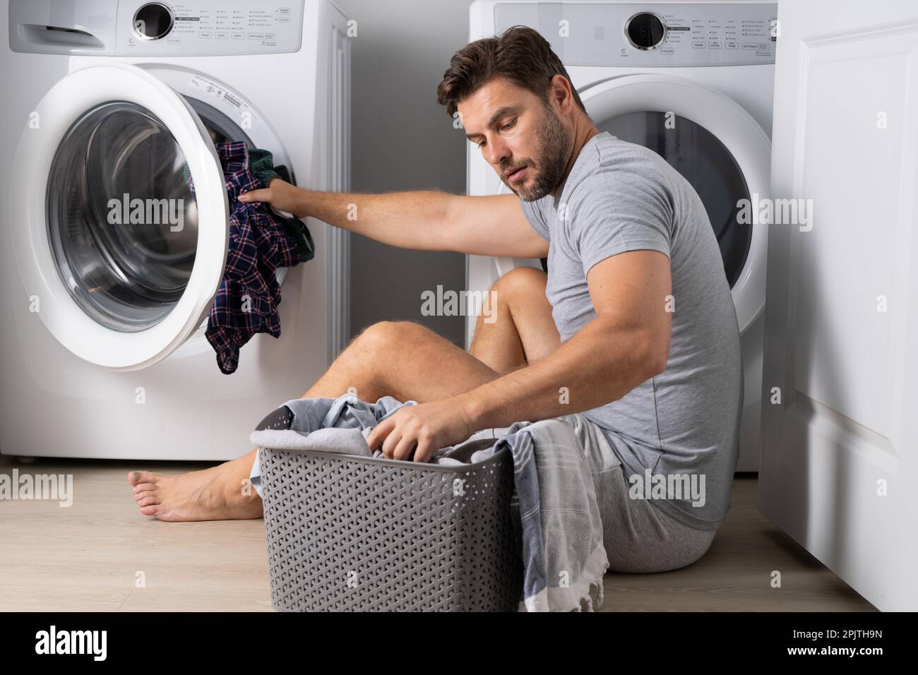 Man loading clothes into washing machine in laundry room. Middle age ...