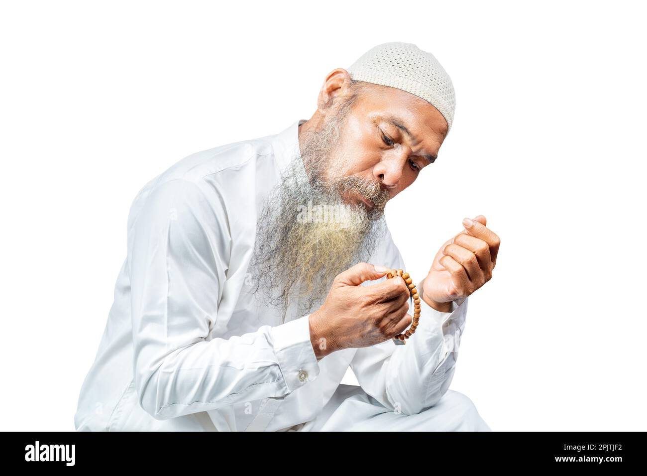Muslim man with a beard wearing a white cap praying with prayer beads ...
