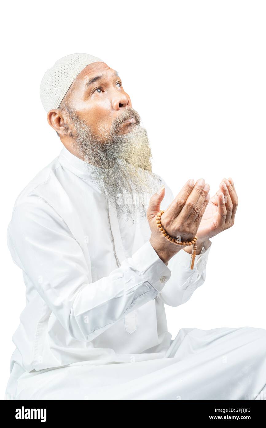 Muslim man with a beard wearing a white cap praying with prayer beads ...