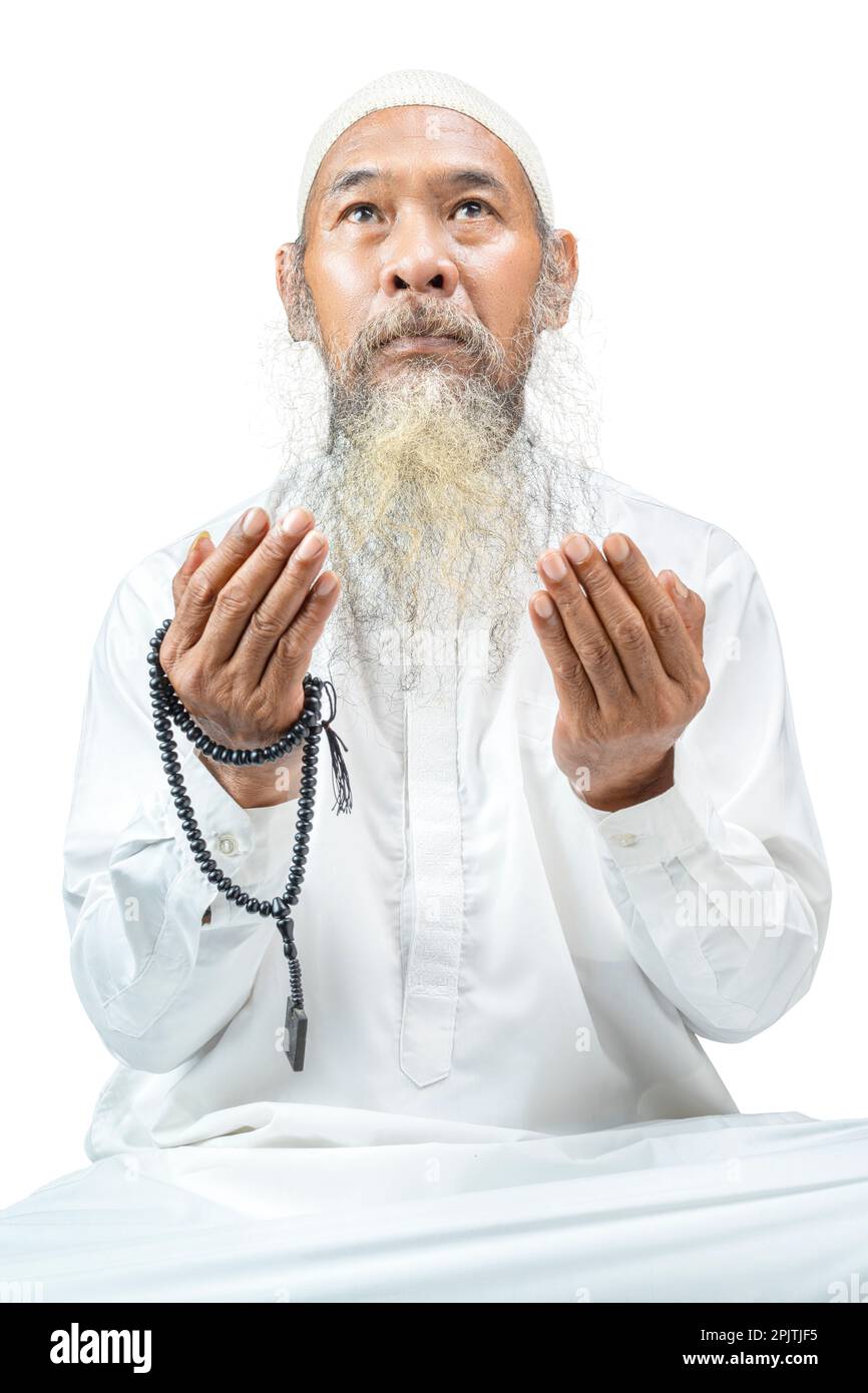 Muslim man with a beard wearing a white cap praying with prayer beads ...