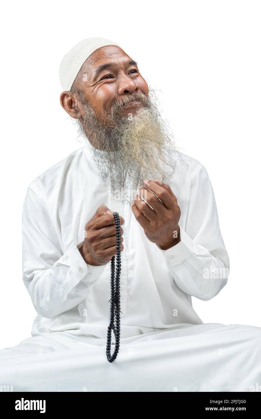 Muslim man with a beard wearing a white cap praying with prayer beads ...