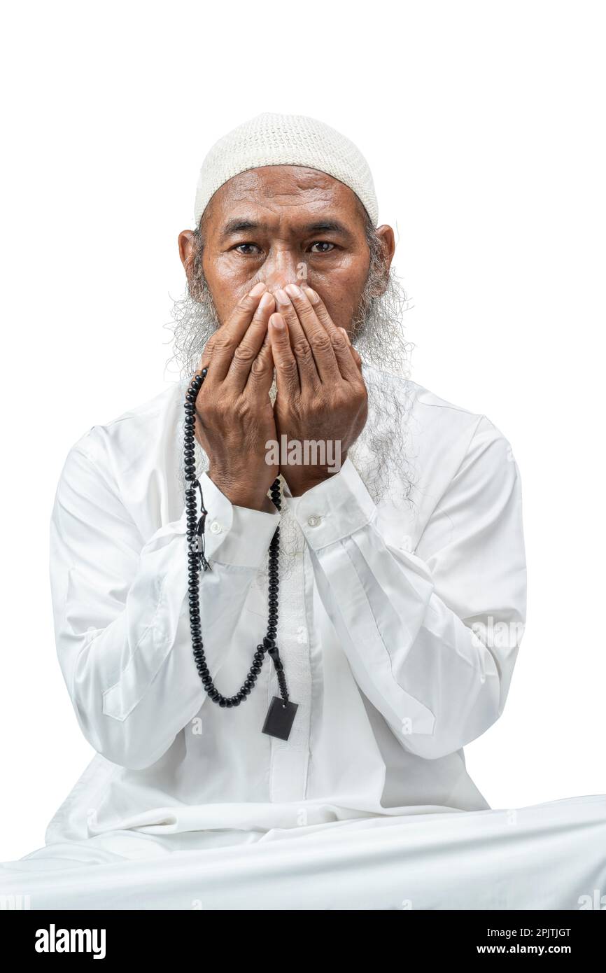 Muslim man with a beard wearing a white cap praying with prayer beads ...