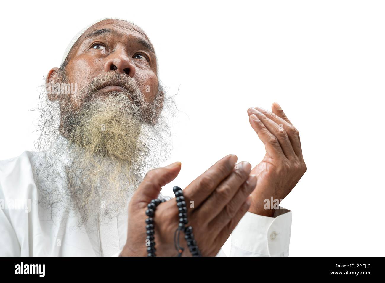 Muslim man with a beard wearing a white cap praying with prayer beads ...