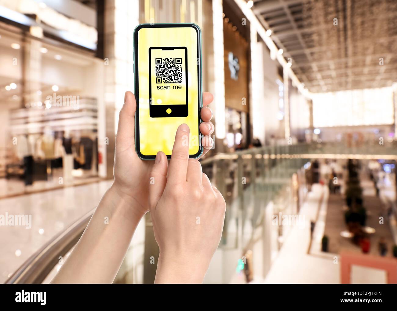 Woman holding smartphone with QR code on screen in shopping mall ...