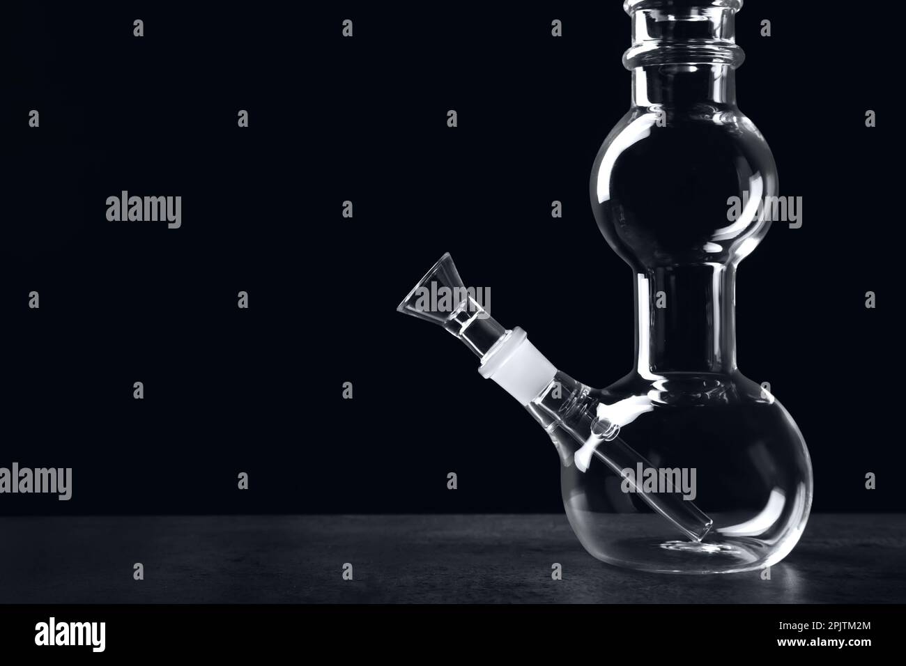 Glass bong on grey table against black background, space for text ...