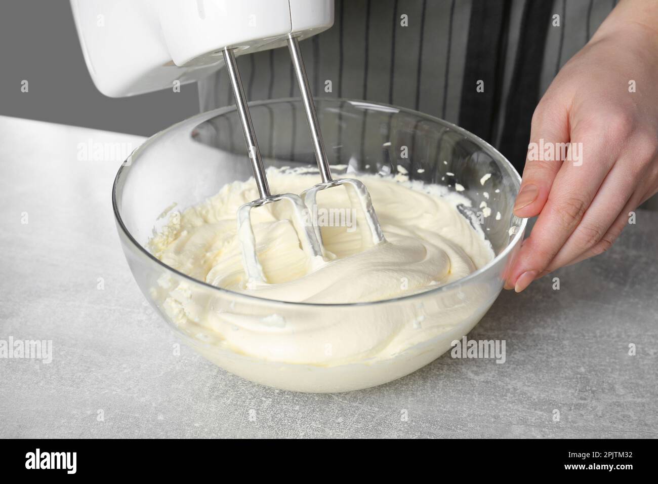 Woman whipping white cream with mixer at light grey table, closeup ...